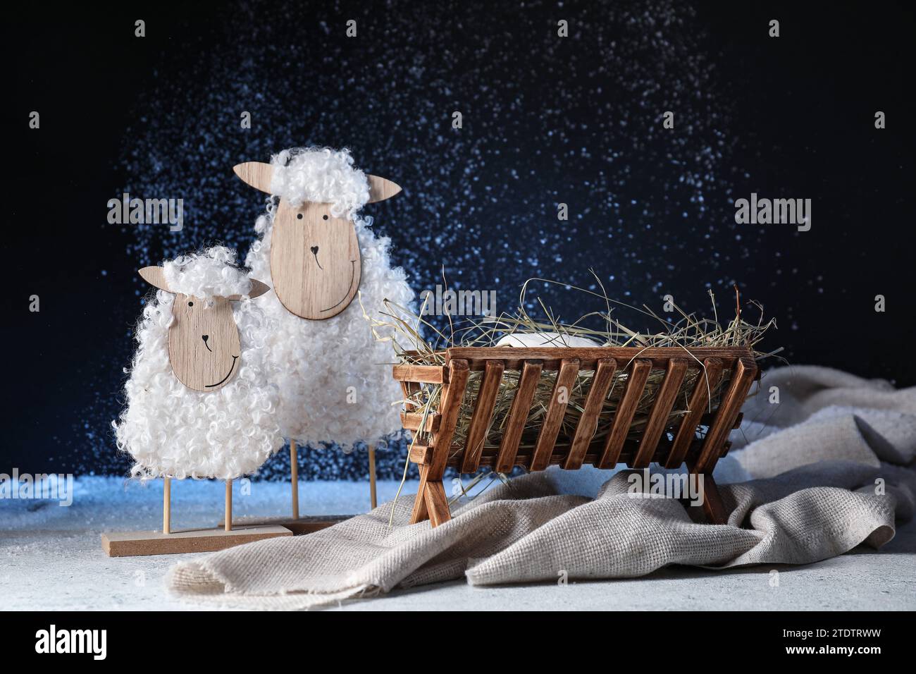 Toy sheep and wooden manger with dummy of baby on snow against black ...