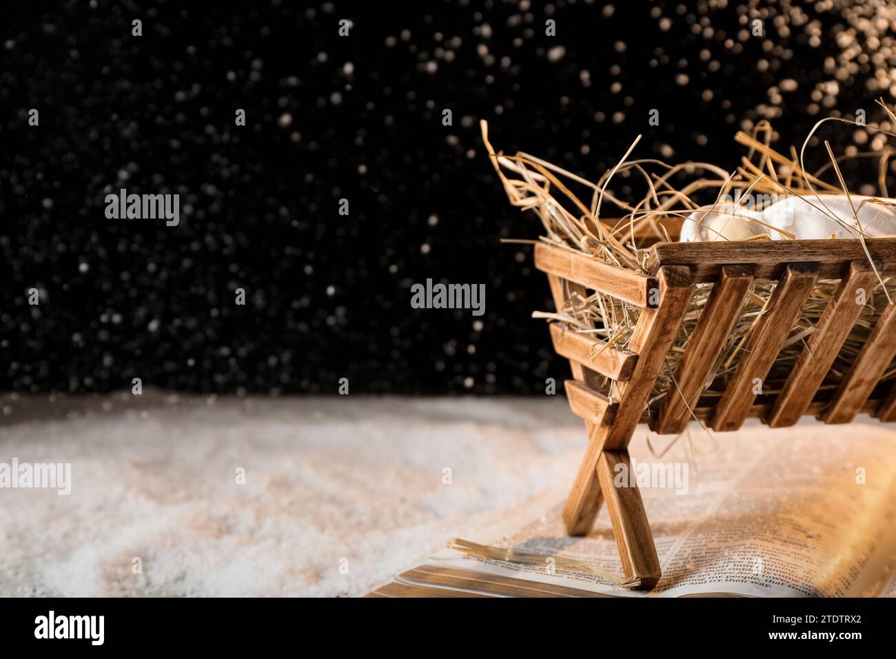 Bible, wooden manger with hay and dummy of baby on snow against black ...