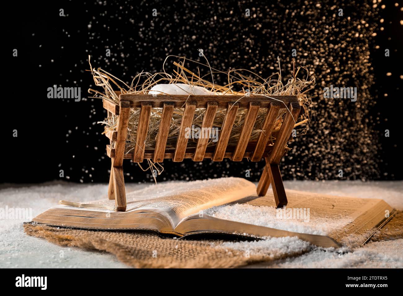 Bible, wooden manger with hay and dummy of baby on snow against black ...