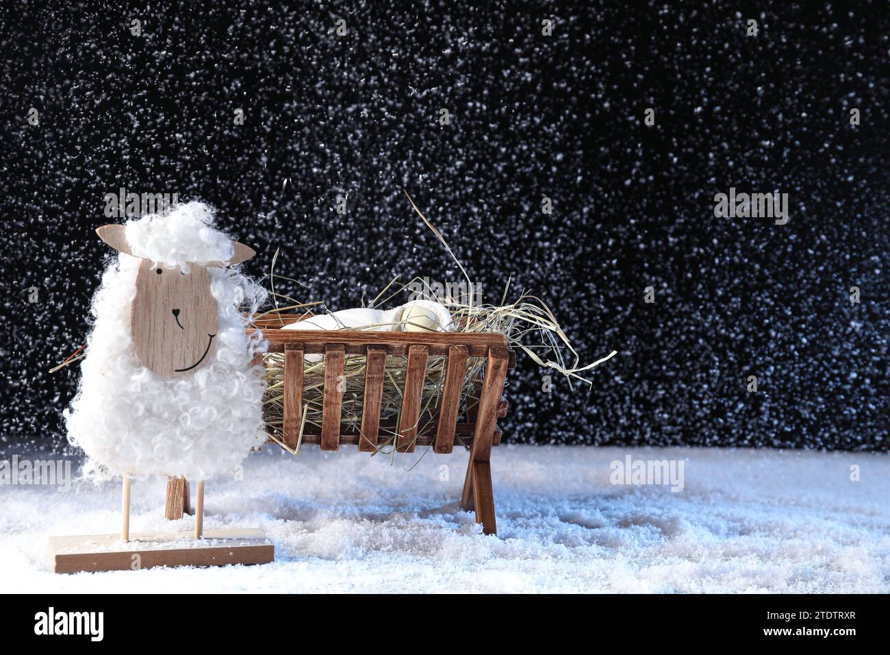 Toy sheep and wooden manger with dummy of baby on snow against black ...