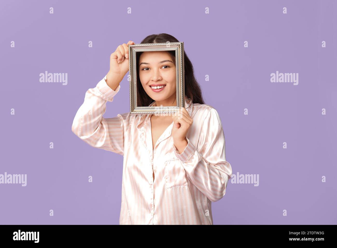 Beautiful young happy Asian woman in pajamas with frame on purple ...