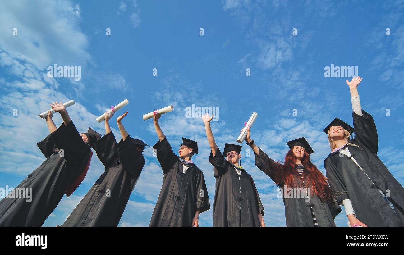 Cheerful graduates pose with raised diplomas on a sunny day Stock Photo ...