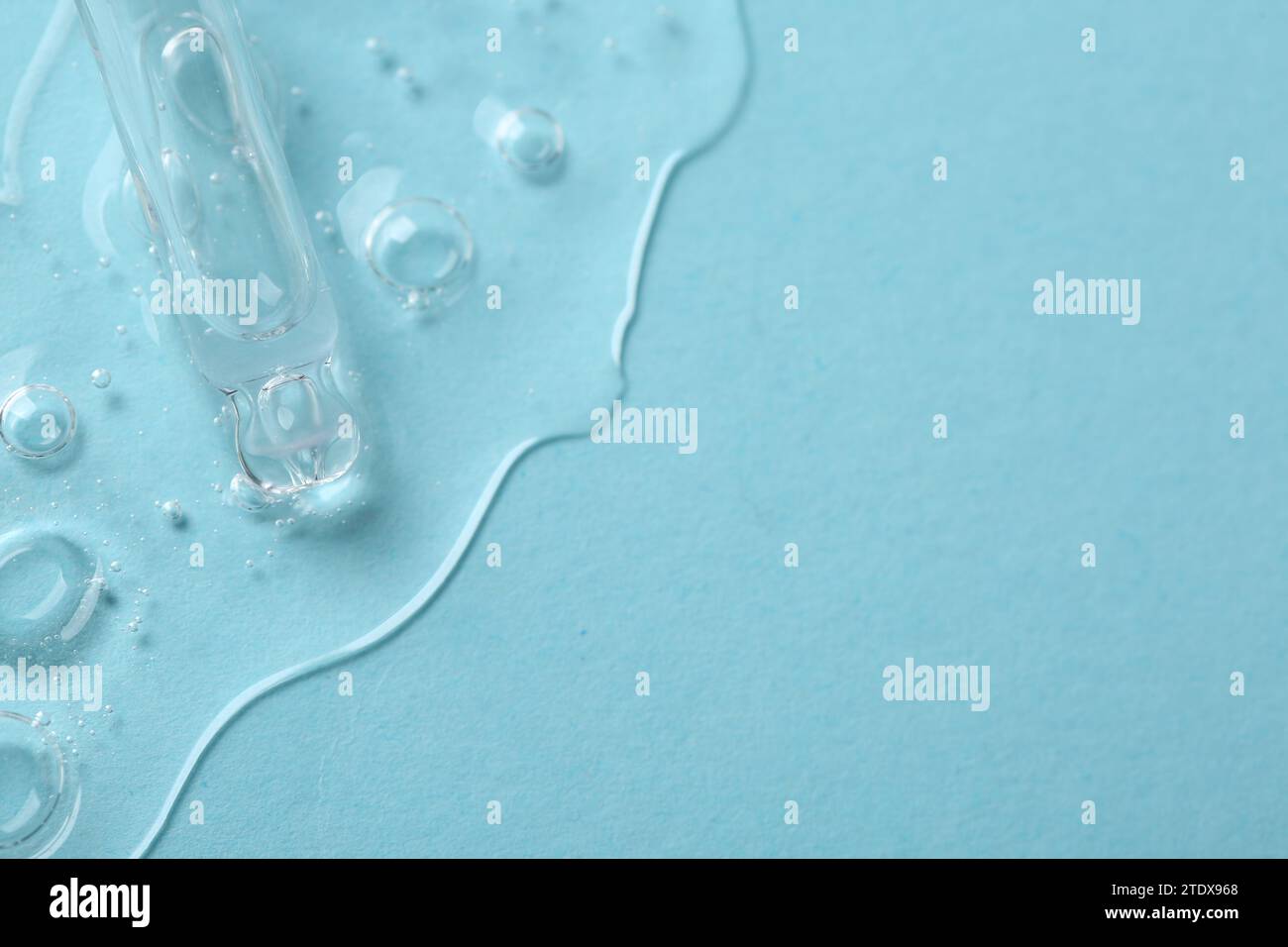 Dripping cosmetic serum from pipette onto light blue background, above ...