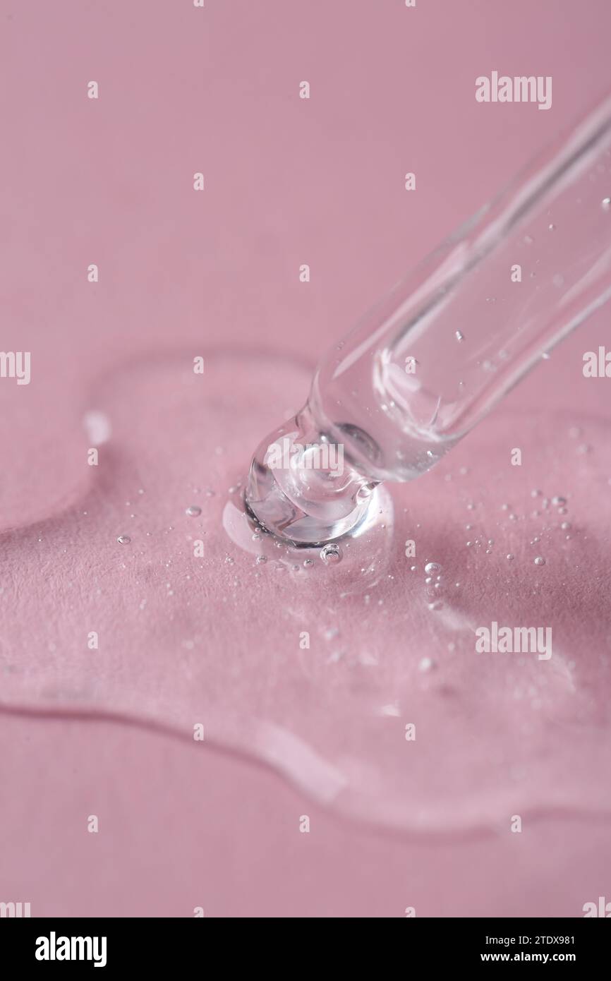 Dripping cosmetic serum from pipette onto pink background, macro view ...
