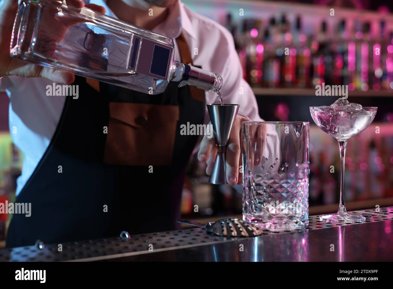 Cocktail making. Bartender pouring alcohol from bottle into jigger at counter in bar, closeup ...