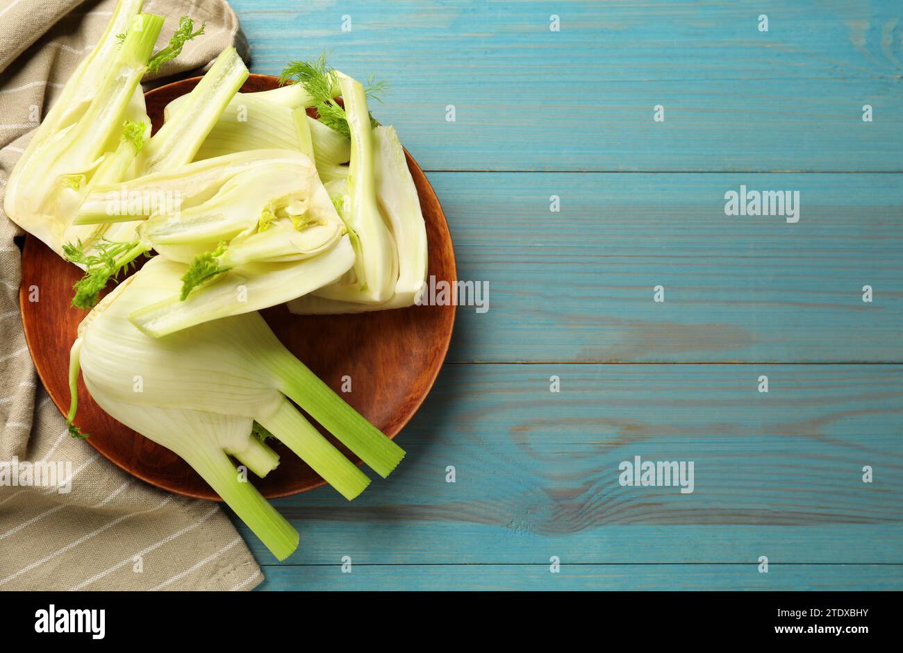 Whole and cut fennel bulbs on light blue wooden table, top view. Space ...
