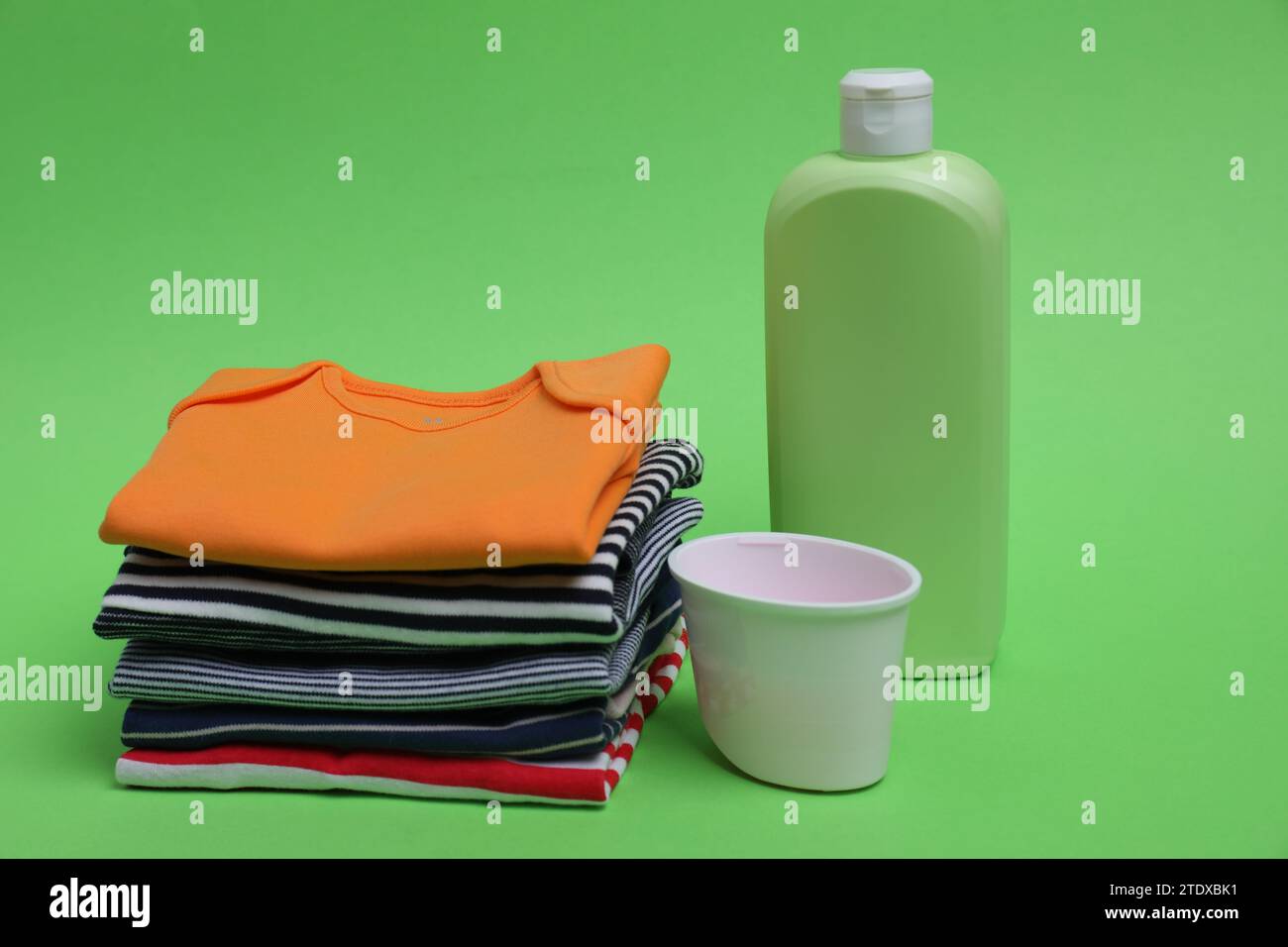 Stack of baby clothes and laundry detergents on light green background ...