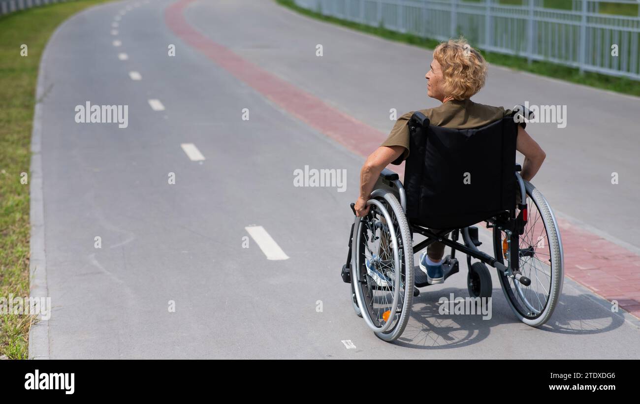 Rear view of an elderly woman in a wheelchair riding on a bike path ...