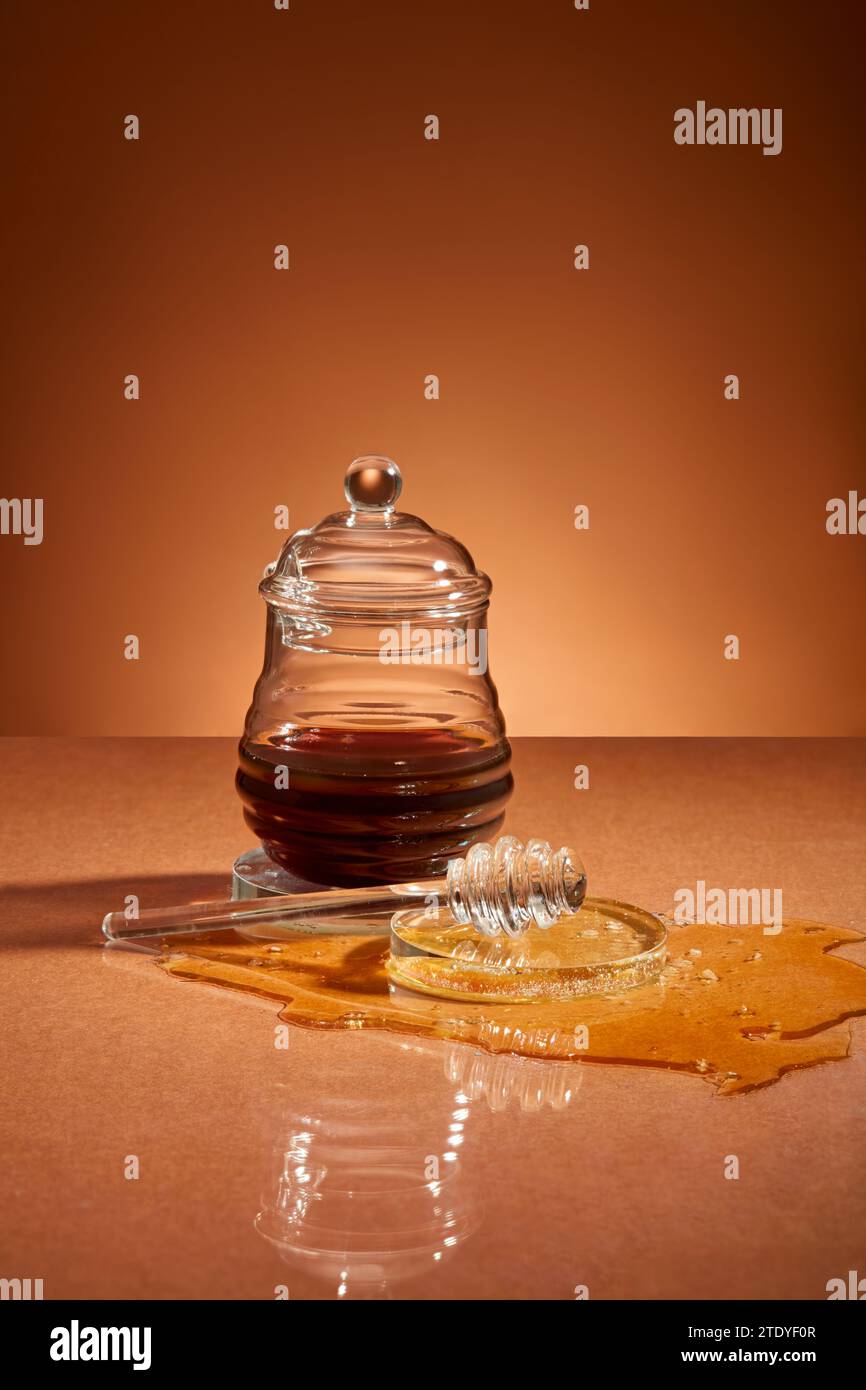 Front view of a glass jar containing honey, honey scattered on a brown ...
