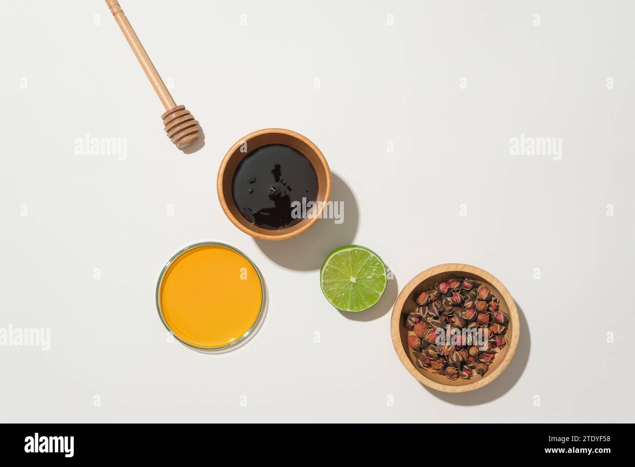 On a white background, wooden bowls cradle honey and dried rose buds ...