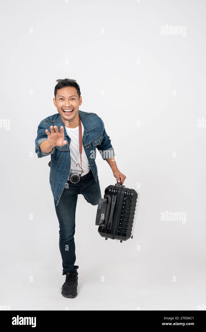 A happy, fun Asian man in jeans jacket is jumping with his travel ...