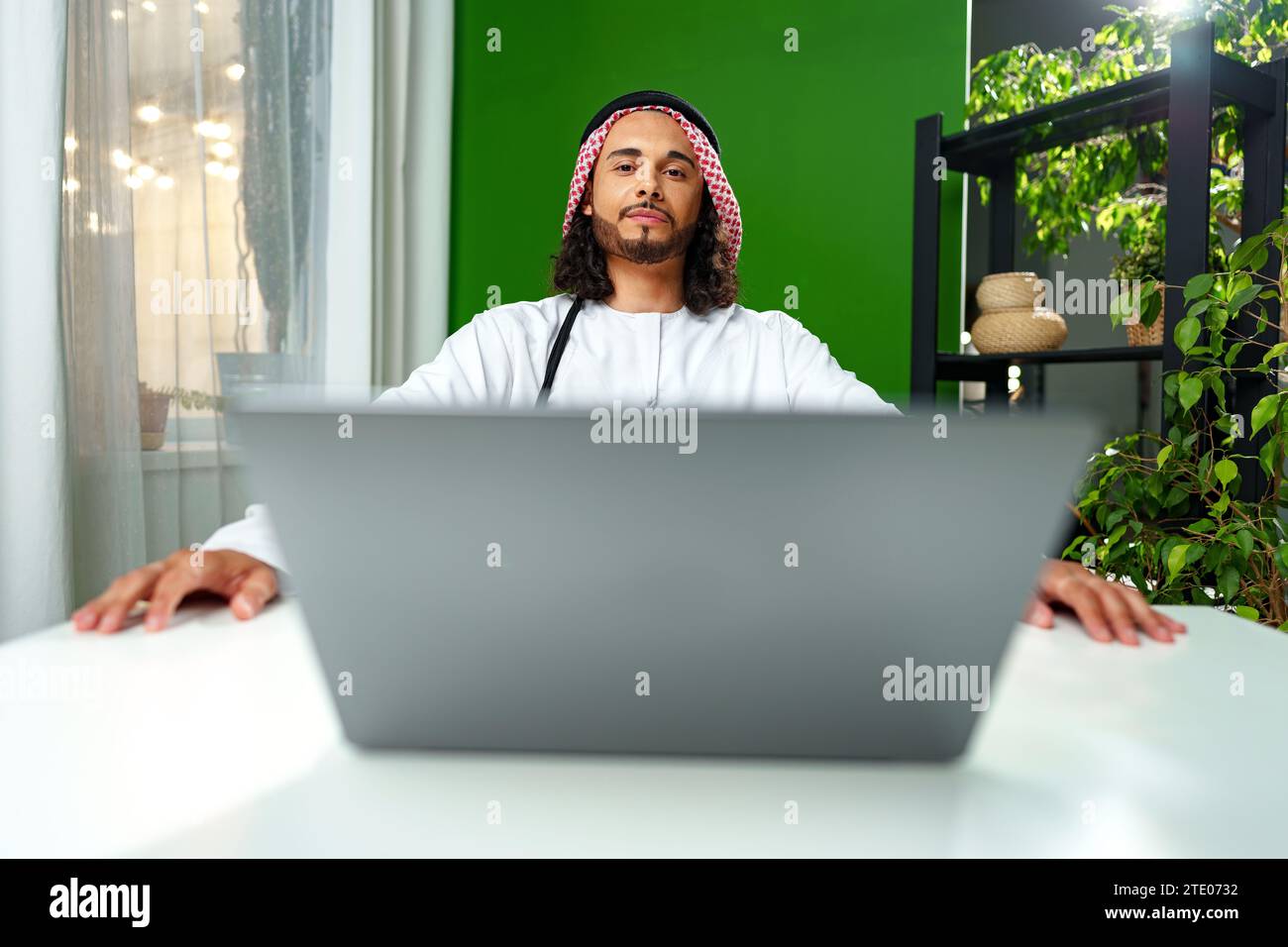 Young Arab man in traditional dress thobe working on computer in office ...