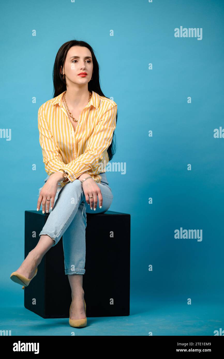Portrait of a girl on a blue background sitting on a black cube Stock ...