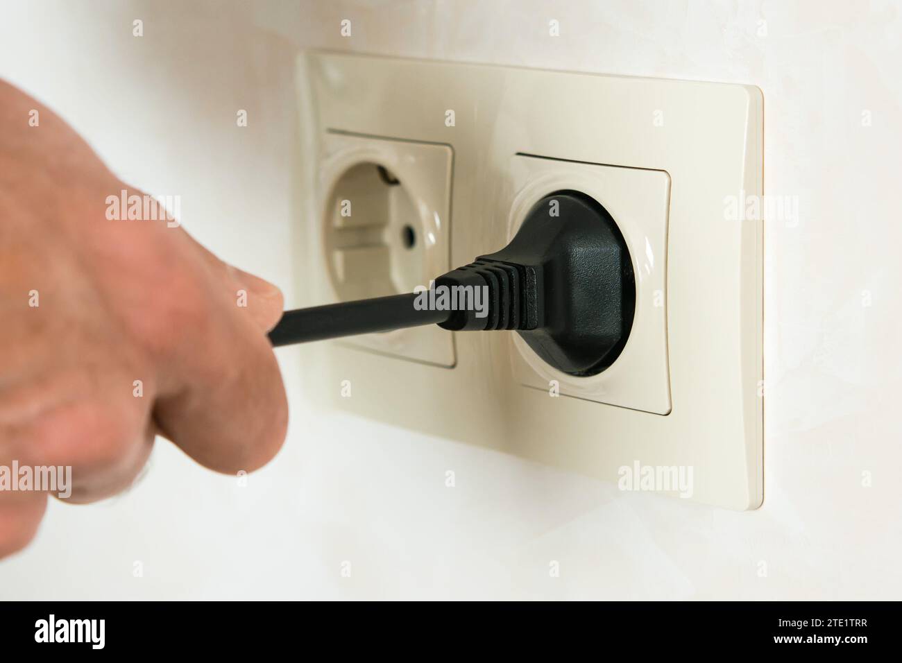 A man's hand holds a power cable by a wire connected to an outlet Stock ...