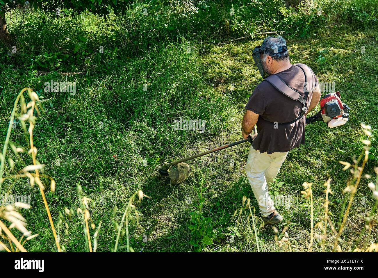 Gardener mowing weeds in the garden with string grass trimmer. Man ...