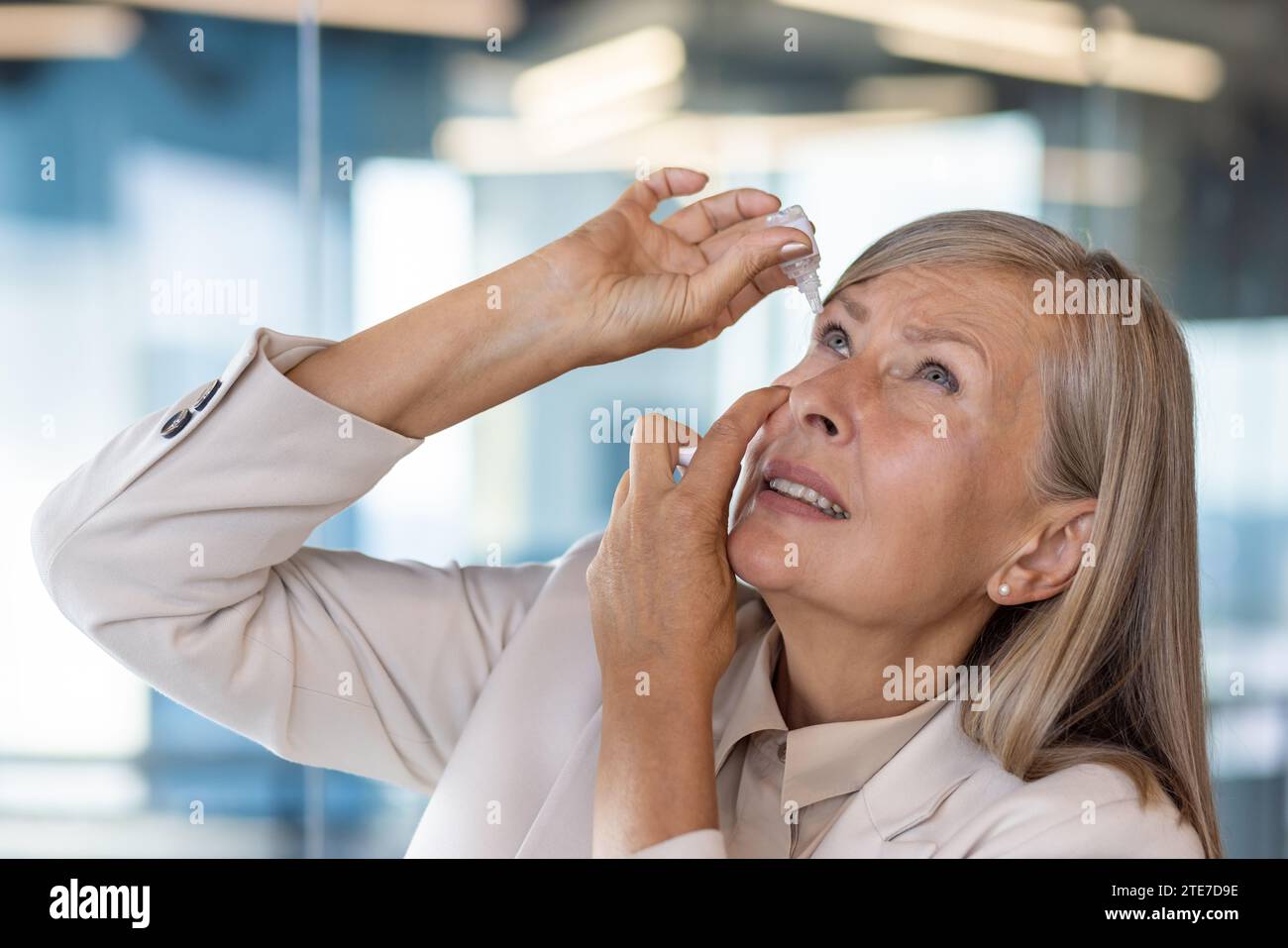 Scared business woman uses eye drops, gray-haired woman overtired sore ...