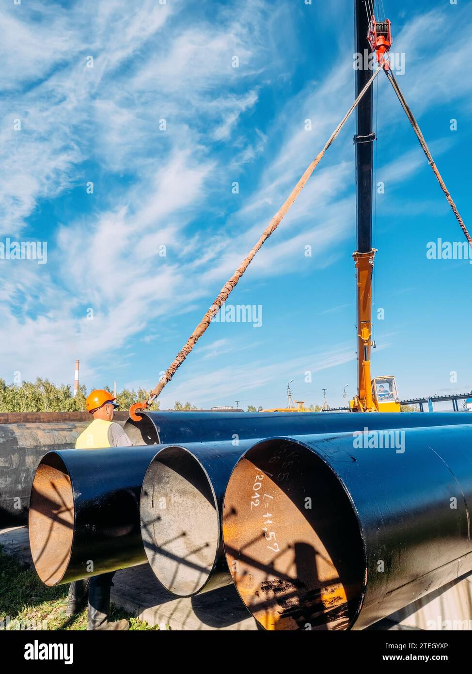 Warehouse of large metal pipes. Worker slinger lays large diameter ...