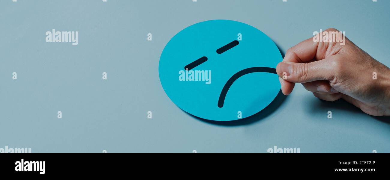 a man is putting a sad mouth to a blue paper face against a gray ...