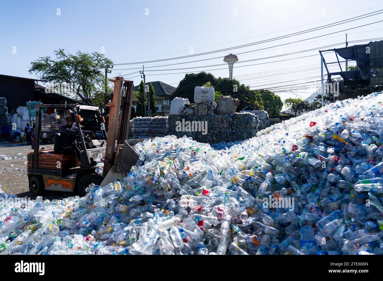 A worker drives a tractor into a large pile of plastic bottles at a ...