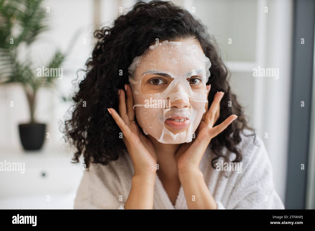 Woman in after-shower outfit touching cosmetic mask fixed on face Stock ...