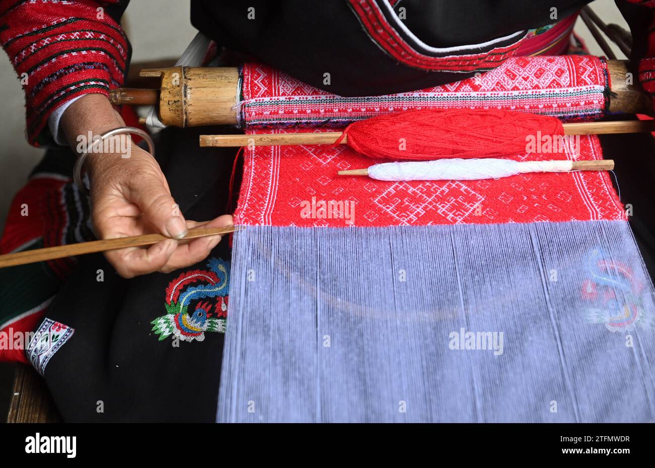 (231220) -- LONGSHENG, Dec. 20, 2023 (Xinhua) -- A villager weaves cloth to make folk costumes ...