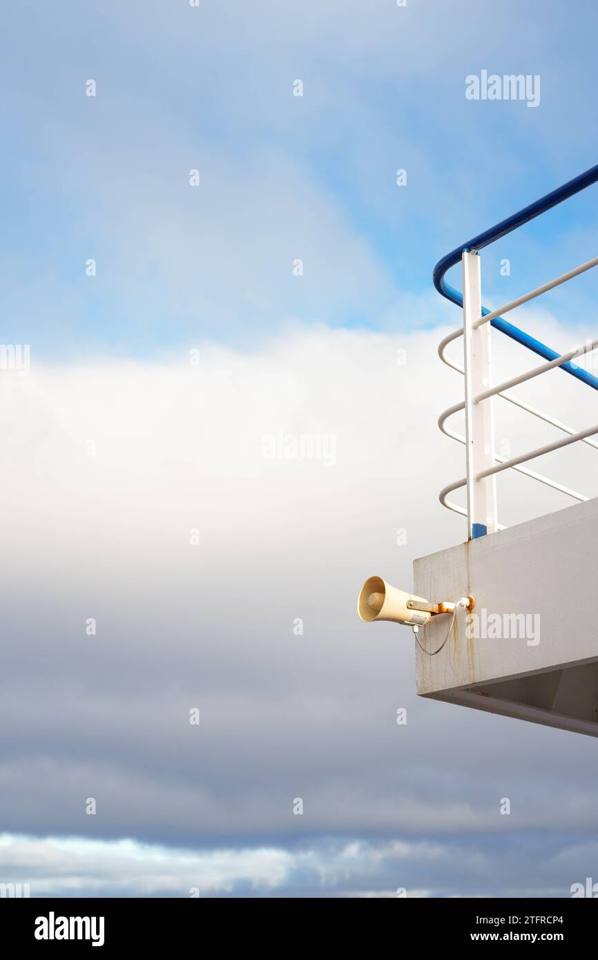 This vertical frame captures a ship horn affixed to a grey deck barrier ...