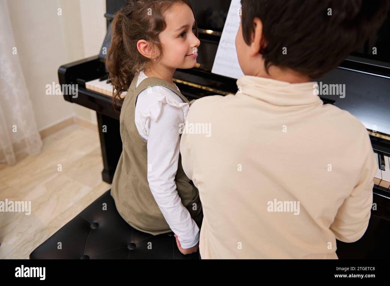 Rear view of two kids playing grand piano together, creating rhythm of ...
