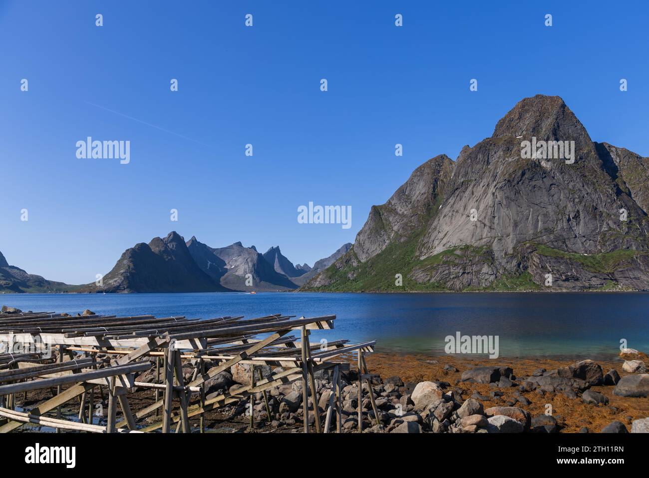 Wooden racks for drying fish frame the serene emerald waters and rugged ...