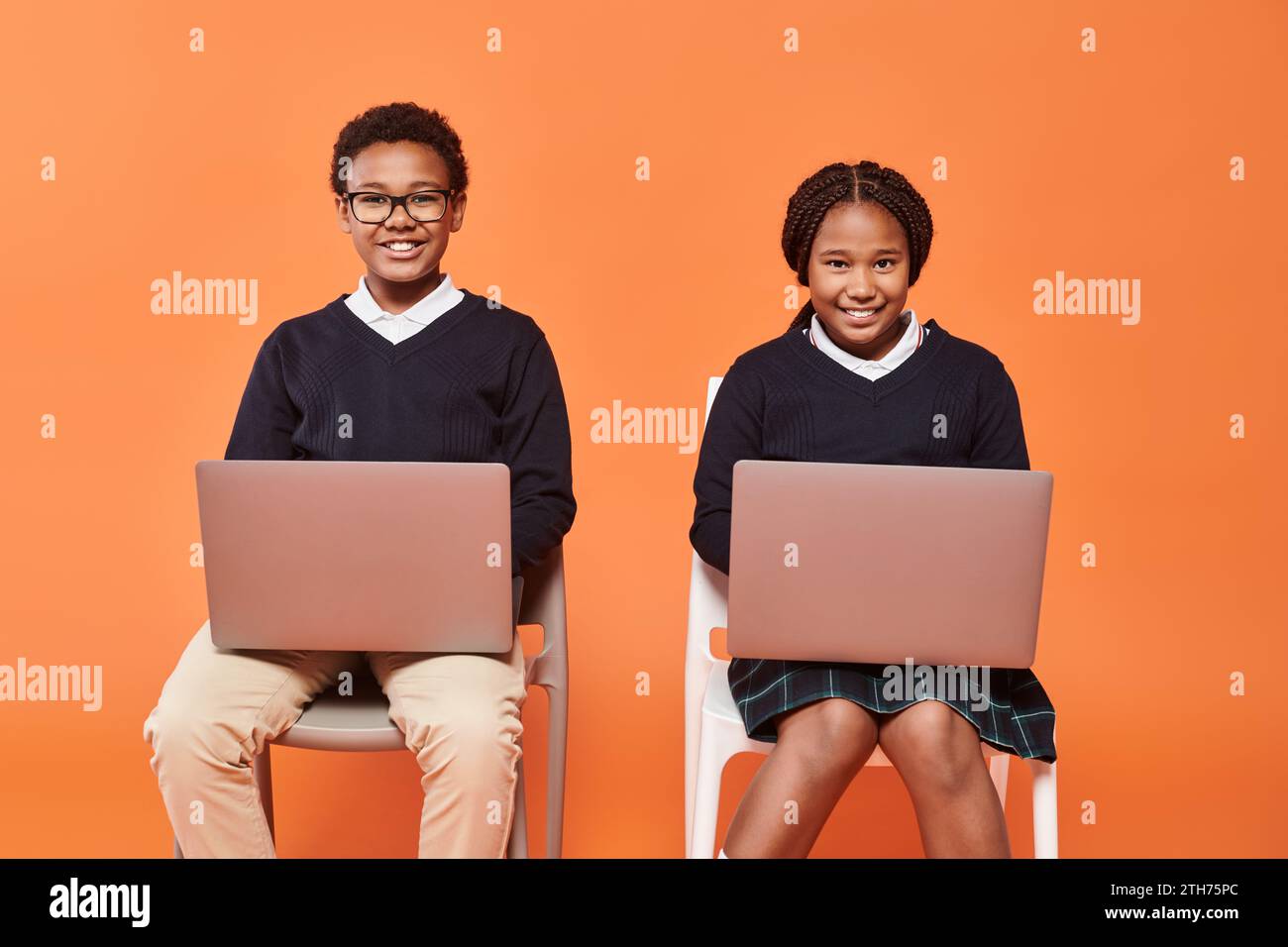 happy african american schoolkids in uniform sitting on chairs and ...