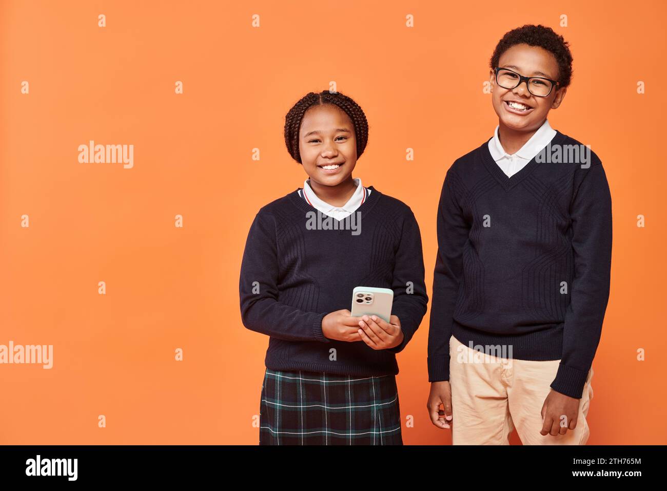 cheerful african american schoolkids in uniform looking at smartphone ...