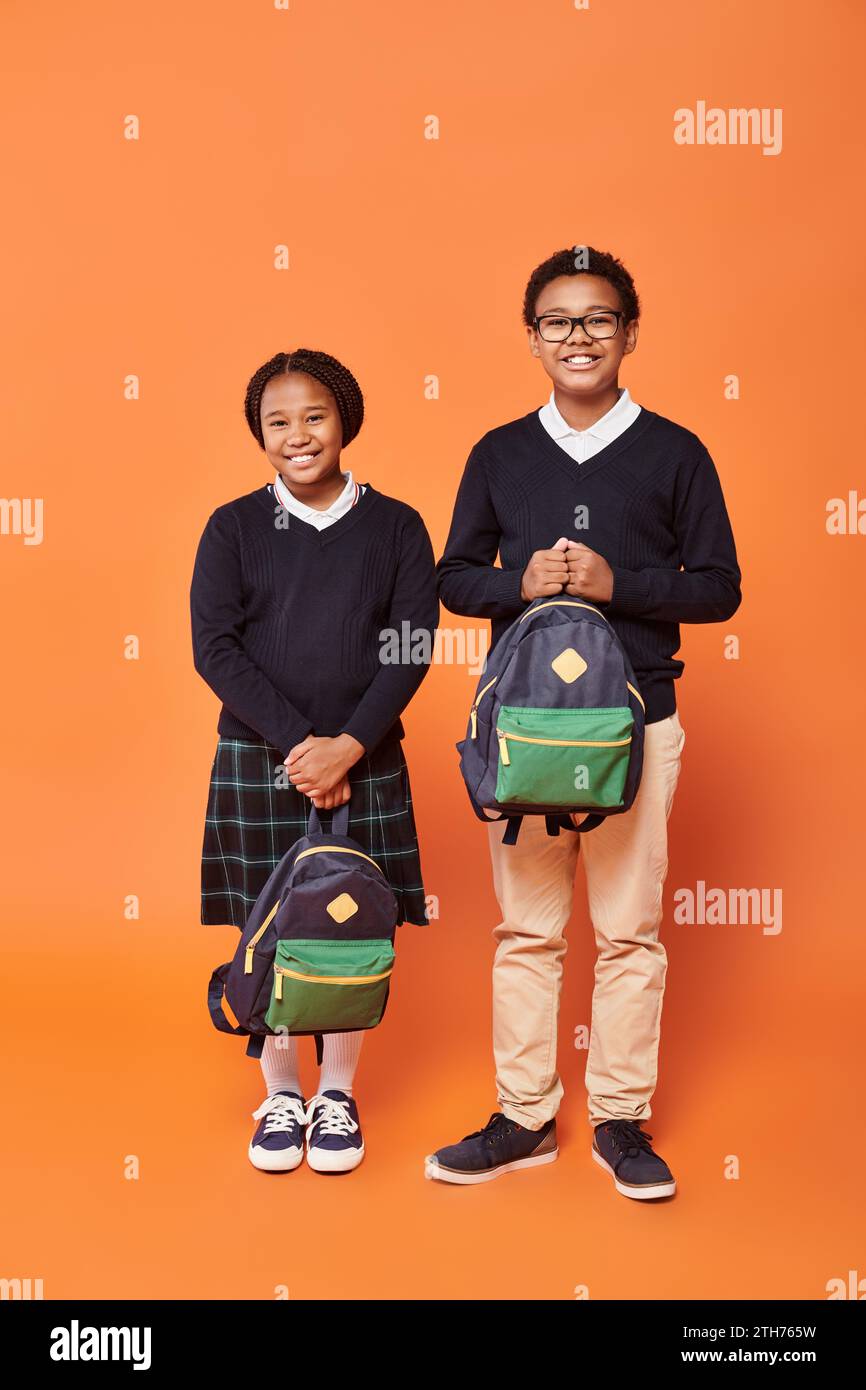 cheerful african american schoolkids in uniform holding backpacks and ...