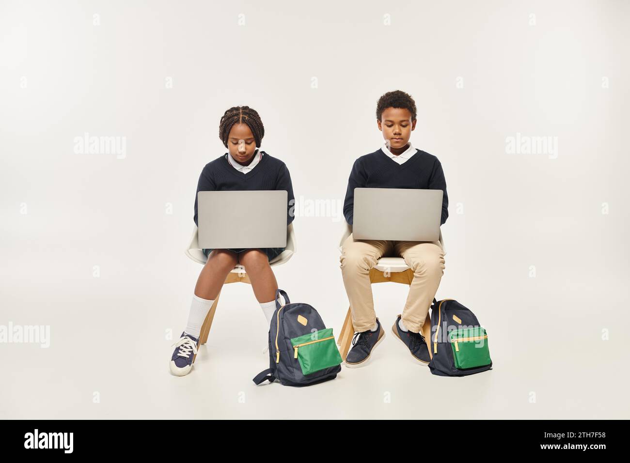 focused african american schoolkids in uniform using laptops and ...