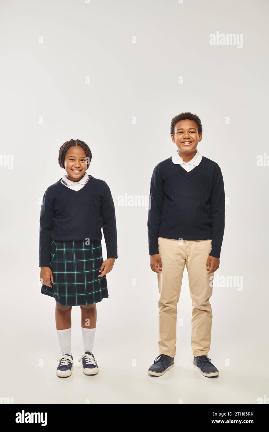 happy african american schoolkinds in uniform posing together on gray ...