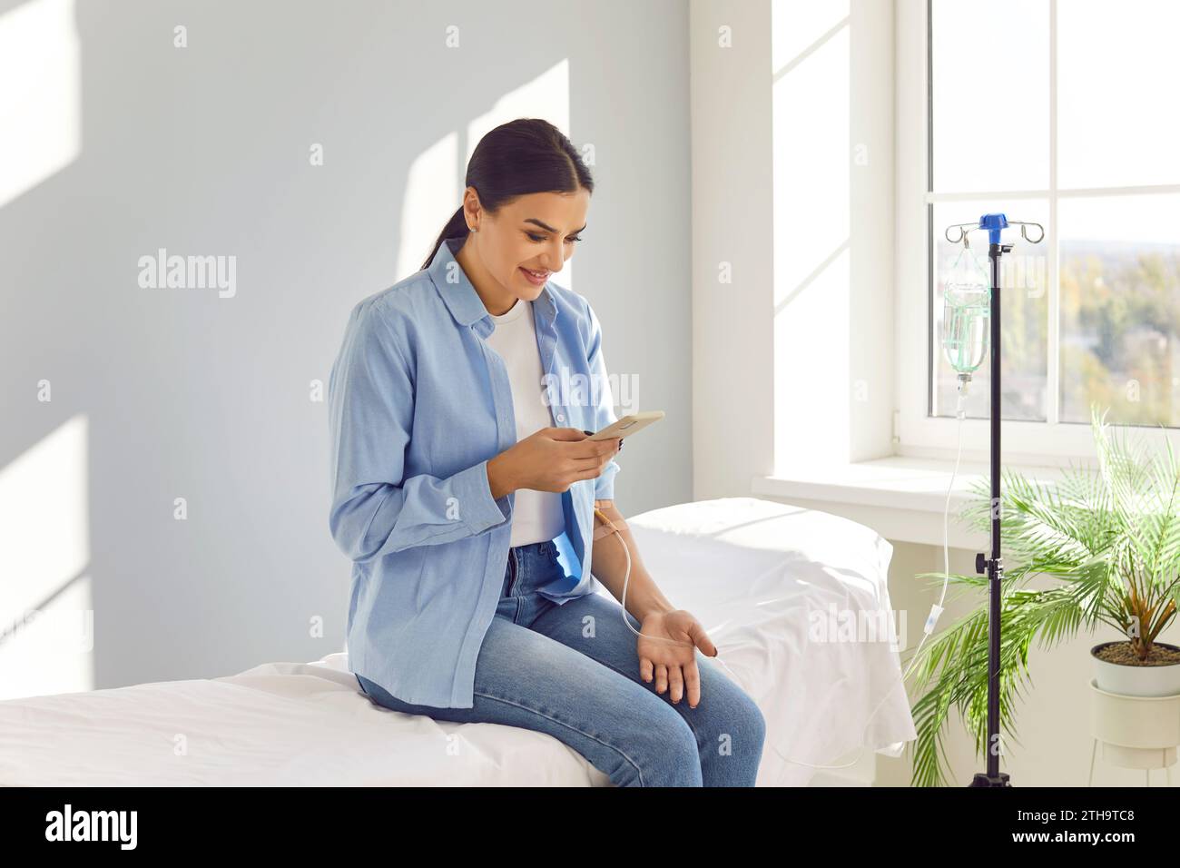 Young smiling woman using smartphone while receiving IV drip infusion ...
