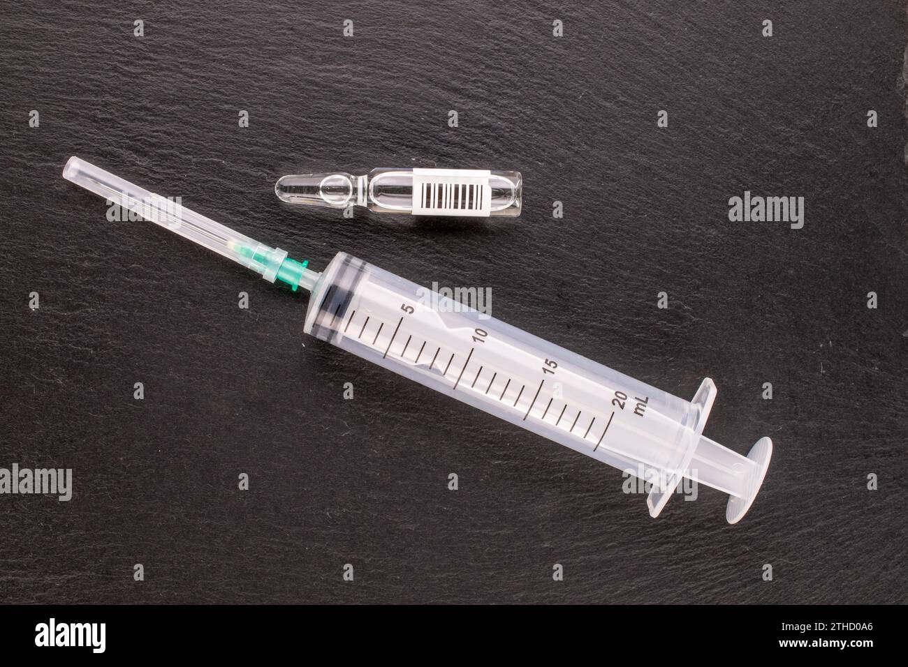 One plastic medical syringe with needle and one glass ampoule on slate ...