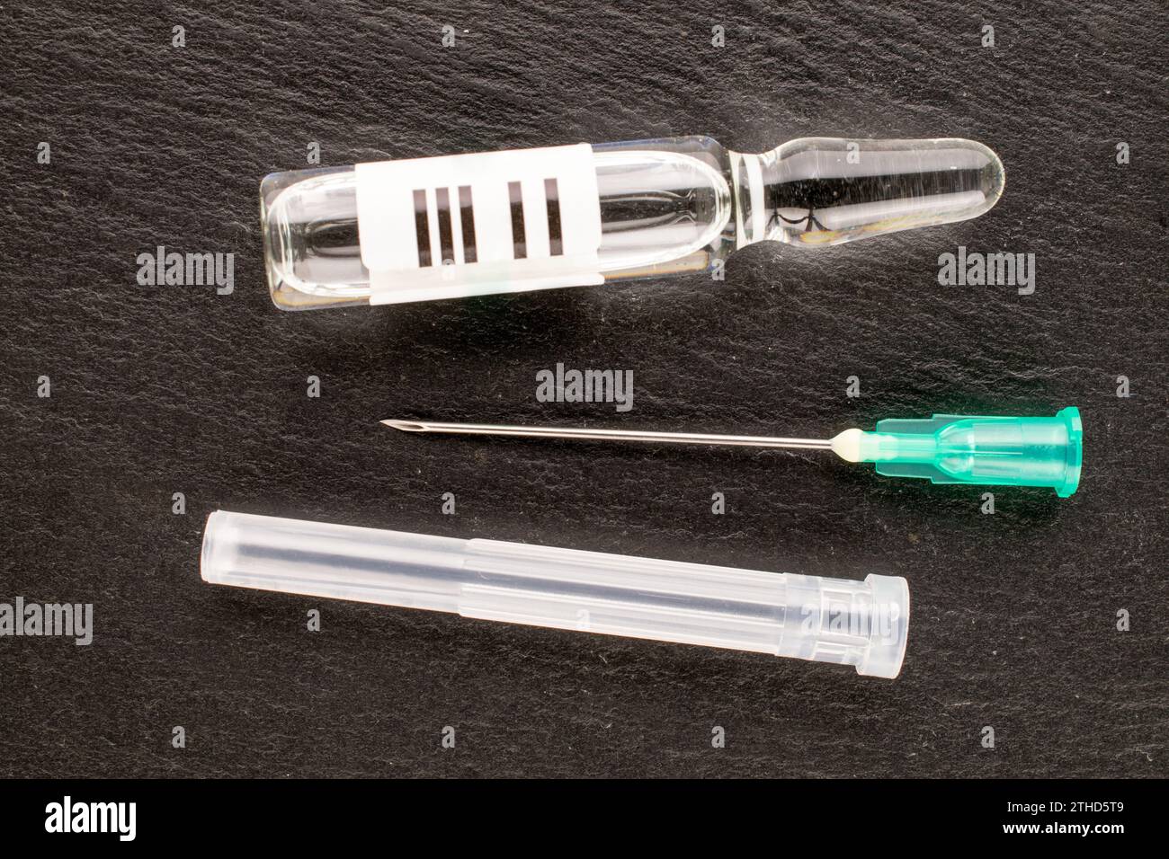 One needle from a medical syringe and one glass ampoule on slate stone ...