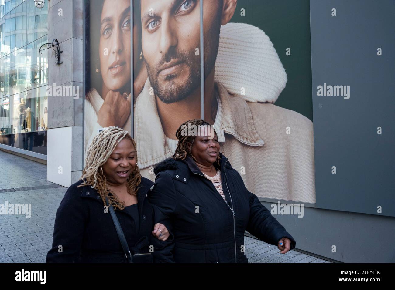 Shoppers and other people pass a large scale poster depicting male and ...
