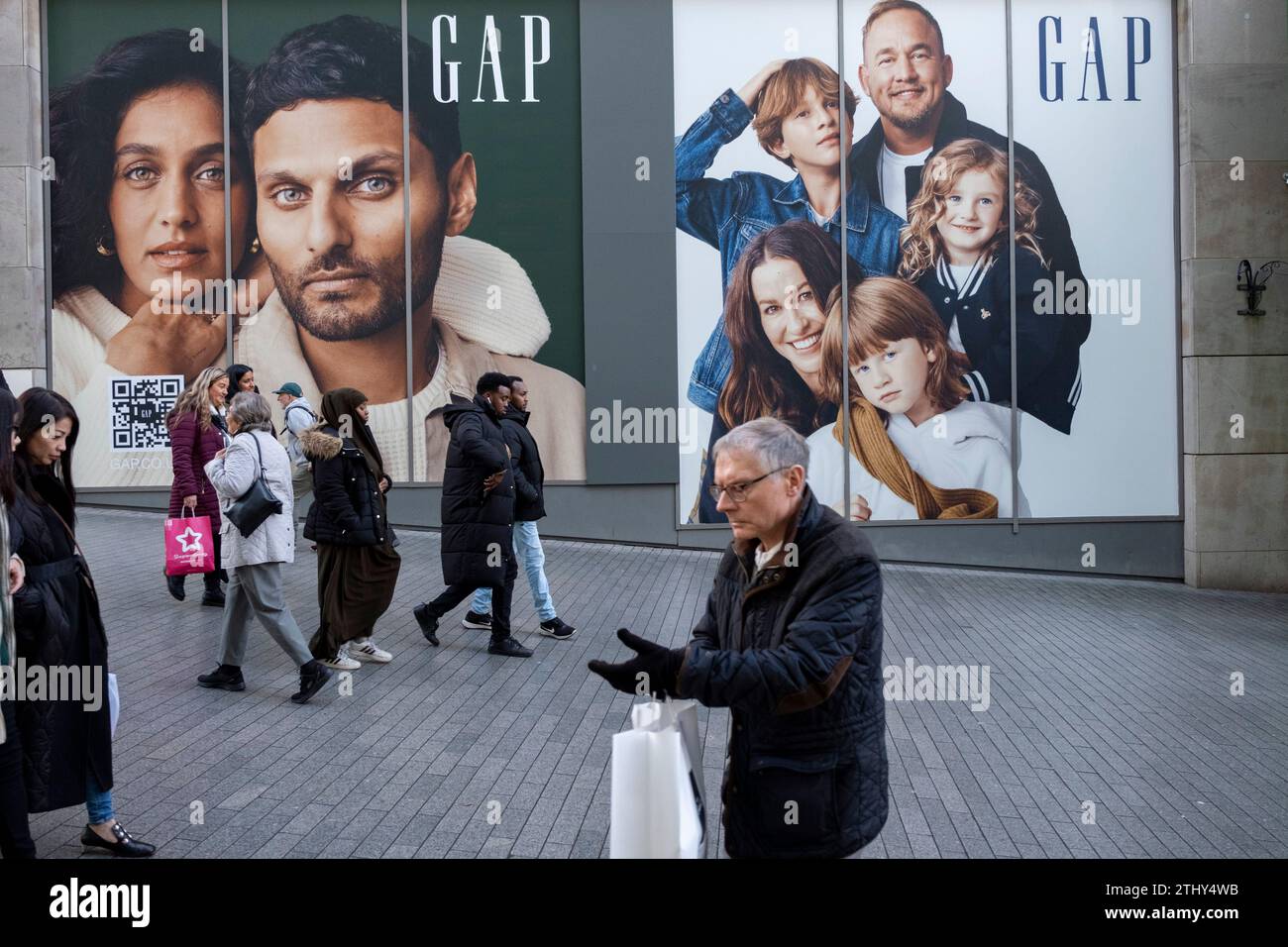 Shoppers and other people pass a large scale poster depicting male and ...