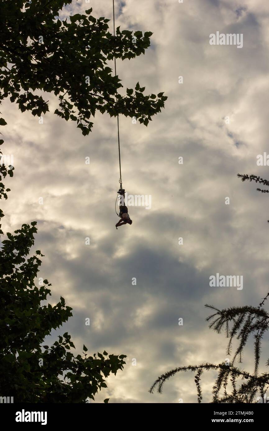 A man tied to a rope upside down doing bungee jump while holding an ...