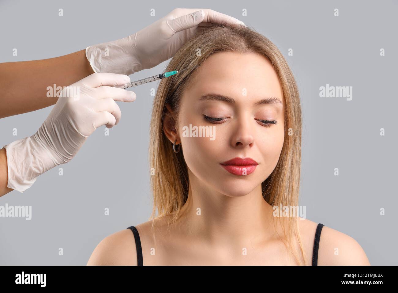 Young woman receiving filler injection in face against grey background ...