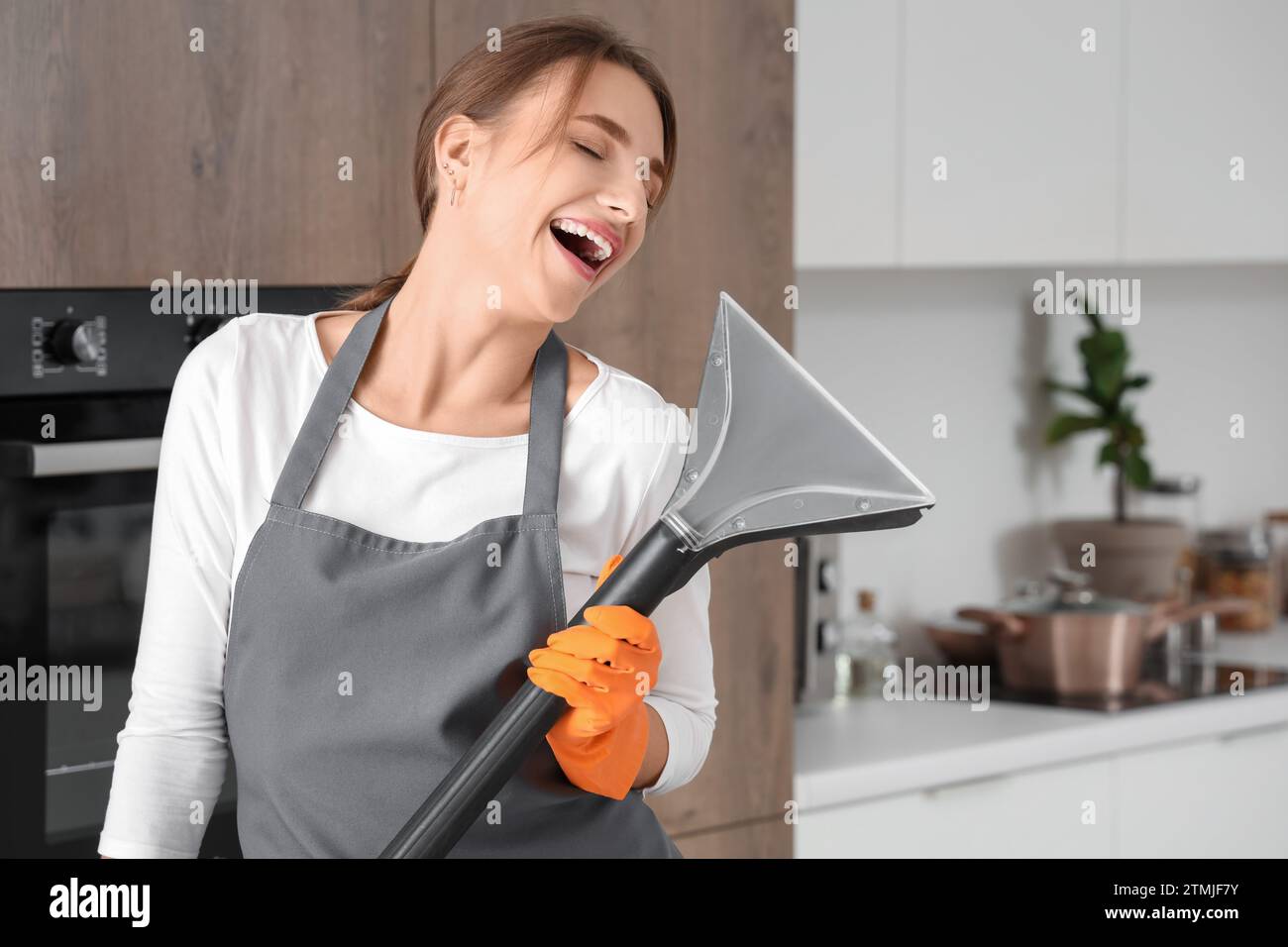 Female janitor with vacuum cleaner singing in kitchen Stock Photo - Alamy