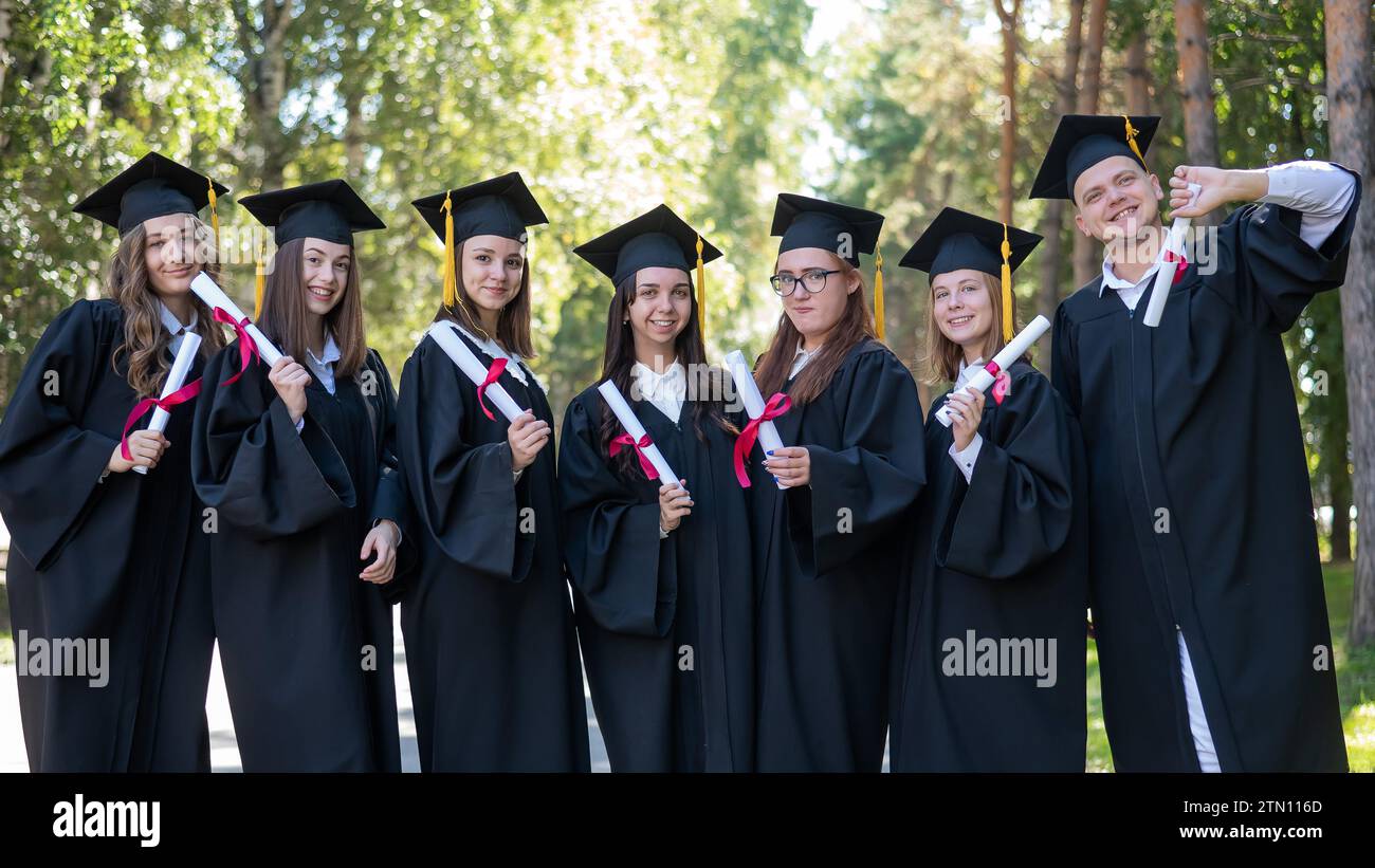 Row of young students in graduation gowns outdoors showing off their ...