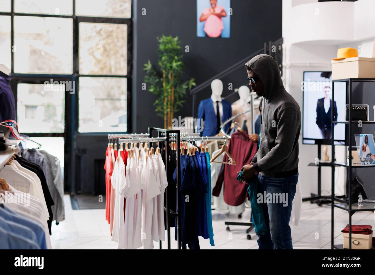 African american thief wearing hood, trying to sneak stolen trendy ...