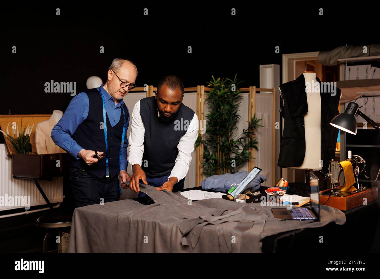 Professional craftsman and apprentice cutting textile material with ...