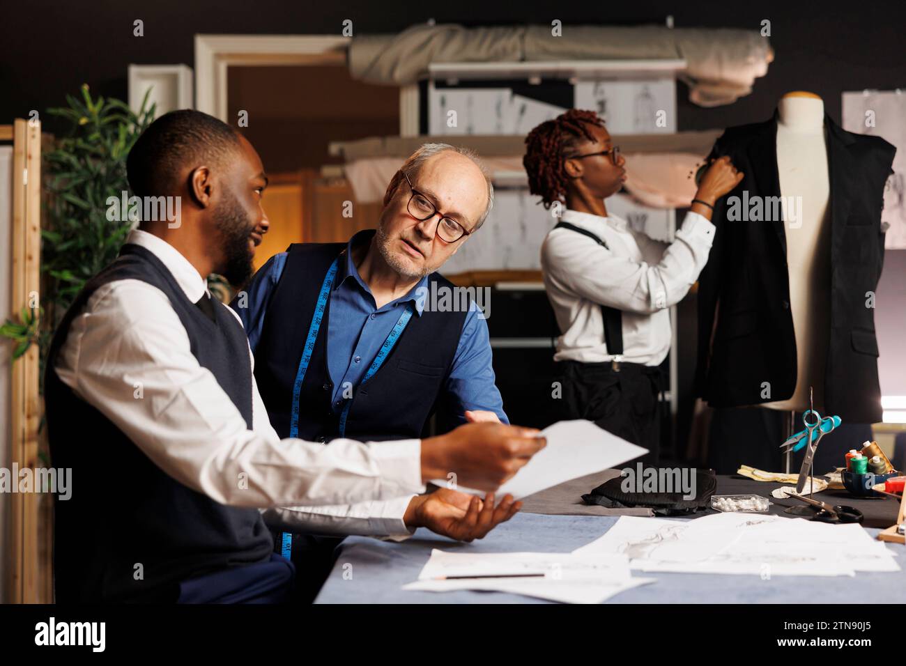 Master tailor working with diverse apprentice team of suitmakers to ...