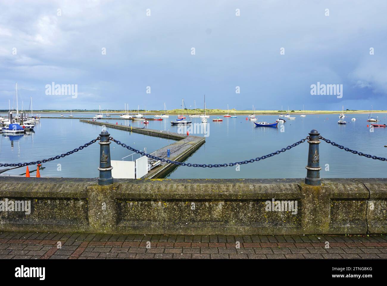 A concrete seawall with iron mooring posts and chain barrier frame a ...