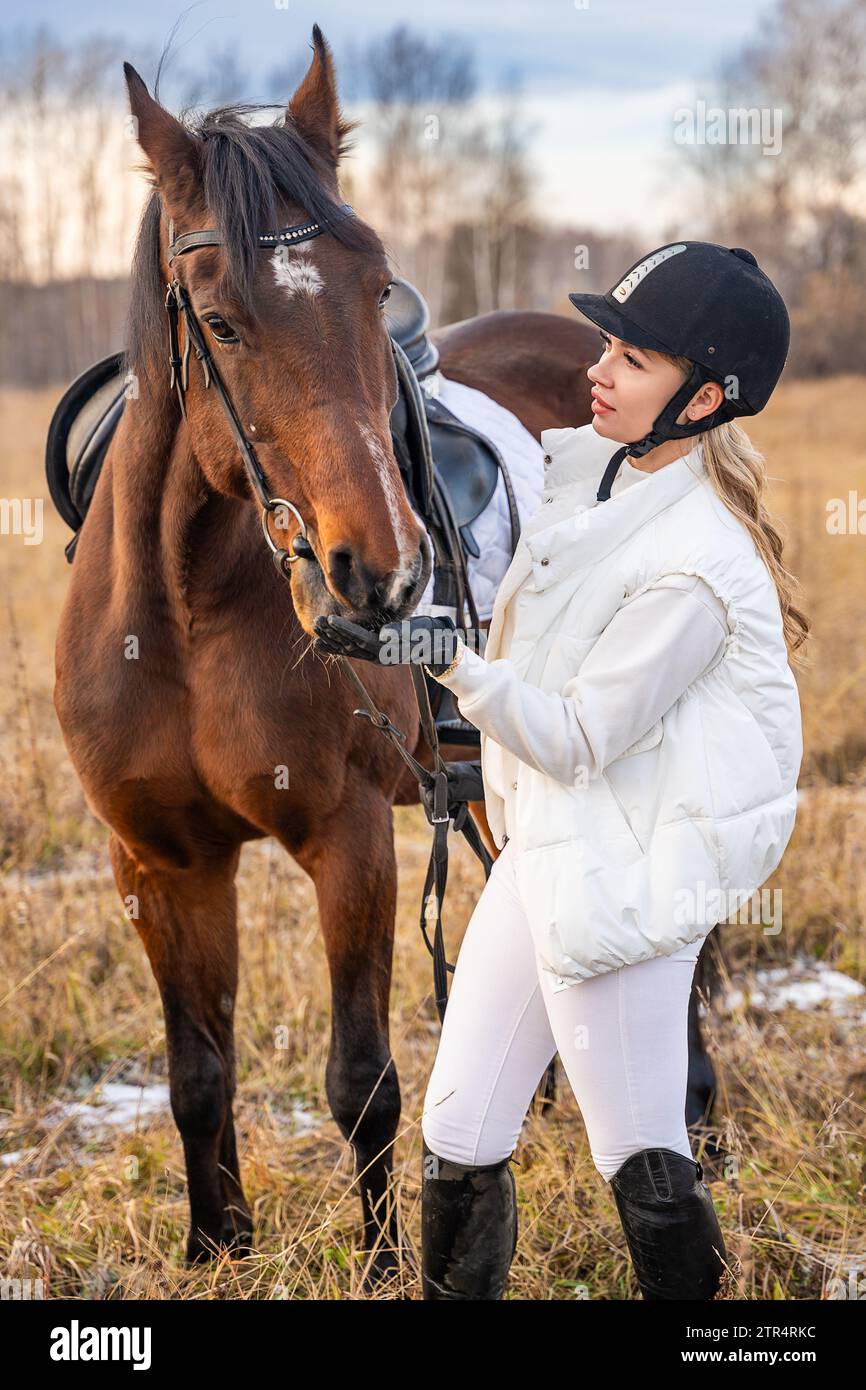 Blond professional female jockey standing near horse in field ...