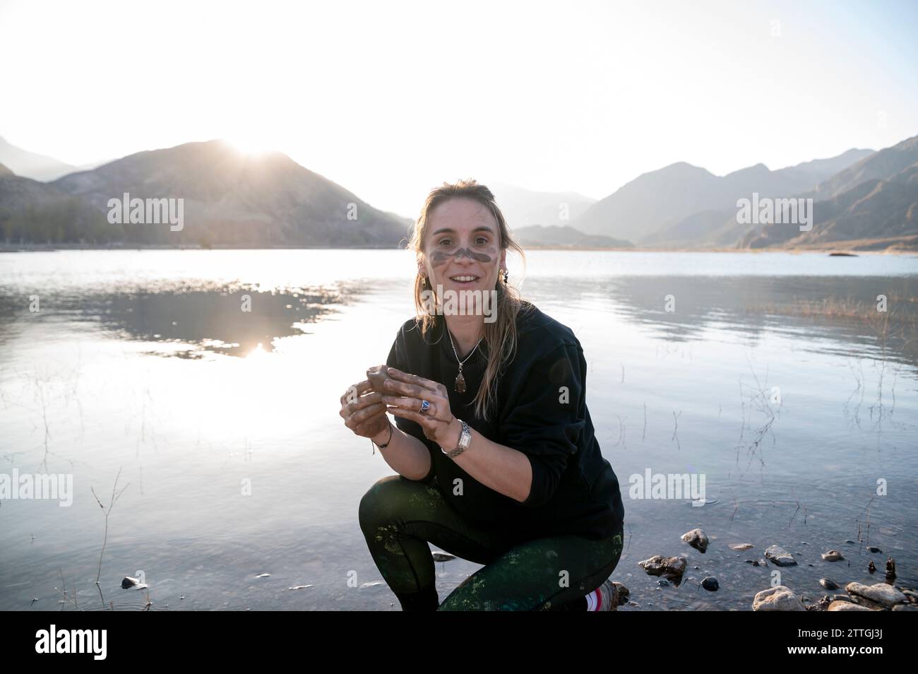 Woman putting mud on hands and face while enjoying outdoors in nature ...