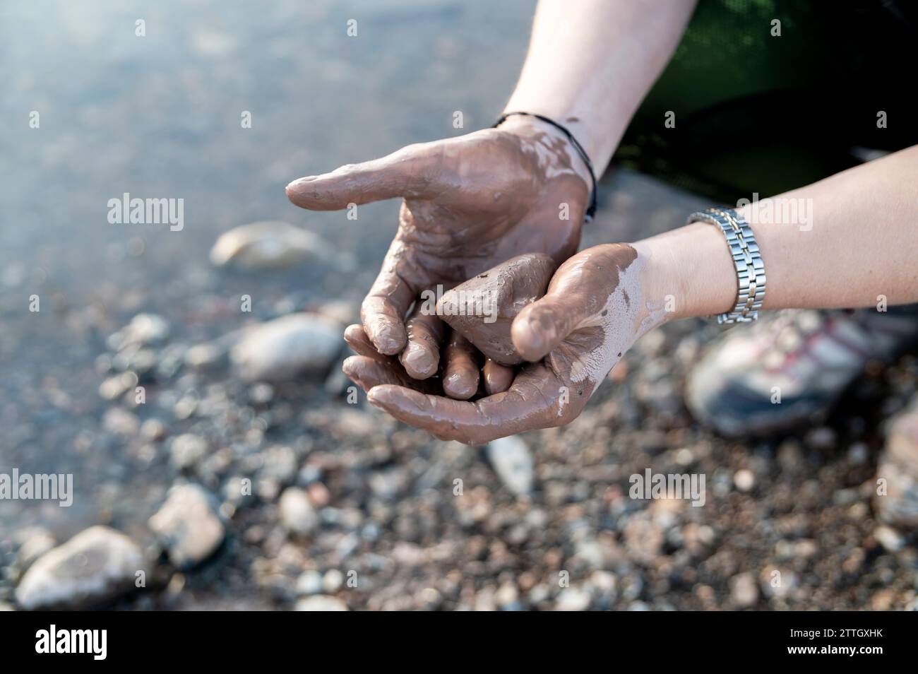 Woman putting mud on hands and face while enjoying outdoors in nature ...