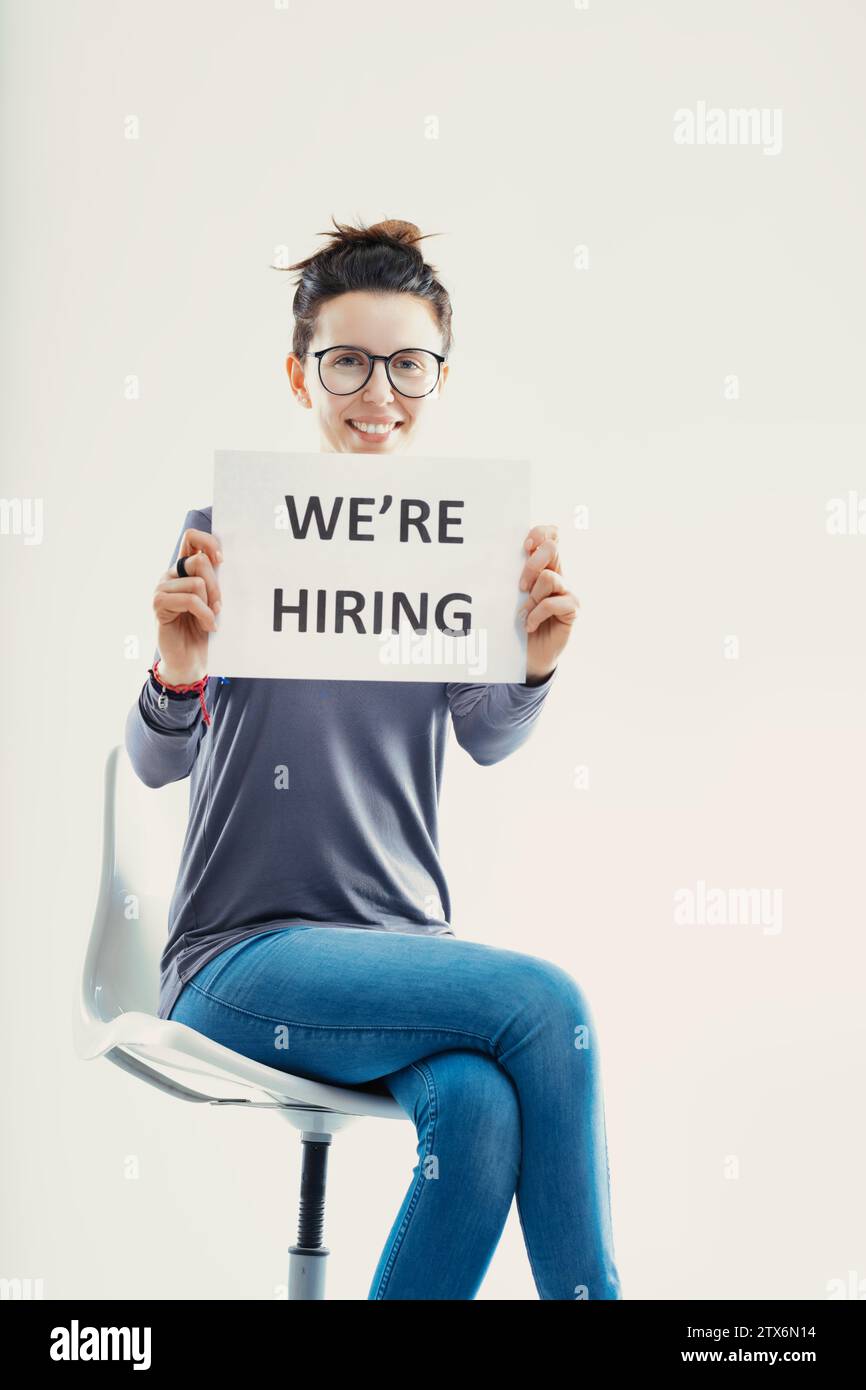 The cheerful individual holds a 'We're Hiring' sign, her bright smile ...
